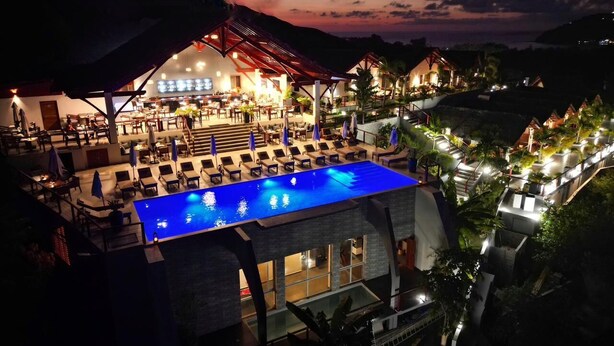 Um resort com piscina, área de estar ao ar livre e montanhas ao fundo.