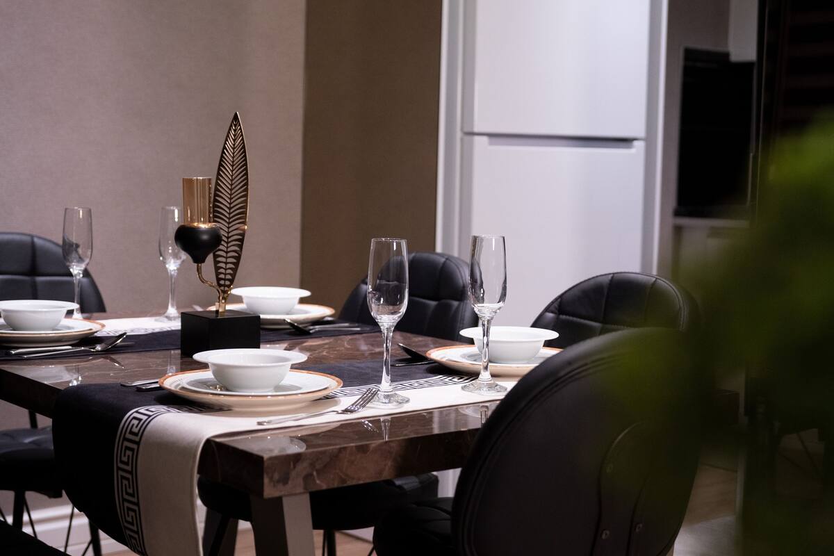 Uma mesa de jantar posta com pratos, copos e talheres, rodeada por cadeiras.
