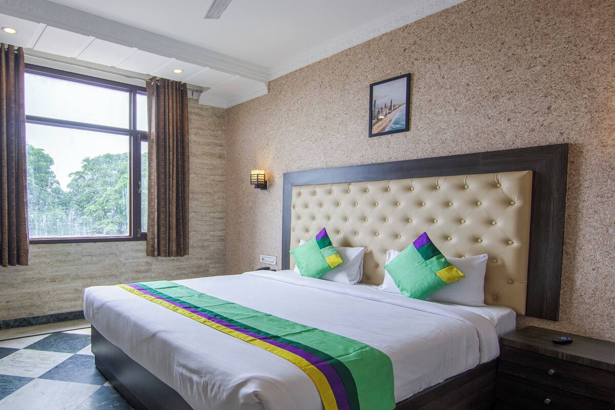 Quarto de hotel com uma cama grande, vista para árvores pela janela e um quadro na parede.