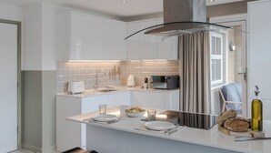 Cozinha moderna com armários brancos, painel de vidro e eletrodomésticos de aço inoxidável.