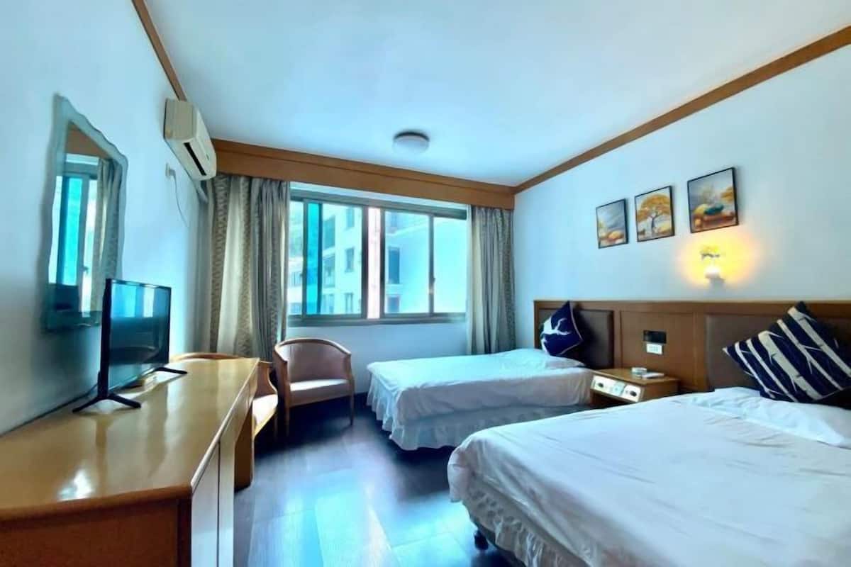 Quarto de hotel com duas camas, uma escrivaninha, uma cadeira, televisão e janela com cortinas.