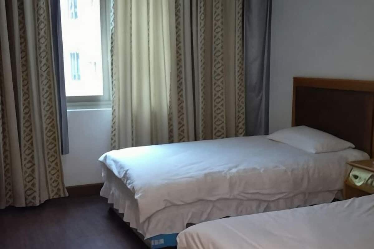 Quarto de hotel com duas camas, uma janela com cortinas e cabeceira de madeira.
