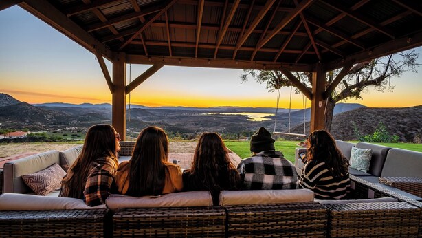 Uma área de estar coberta ao ar livre, com vista para um vale e montanhas.