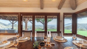 Mesa de jantar posta para quatro com copos de vinho, pratos e uma garrafa de vinho, com vista para uma paisagem deslumbrante.