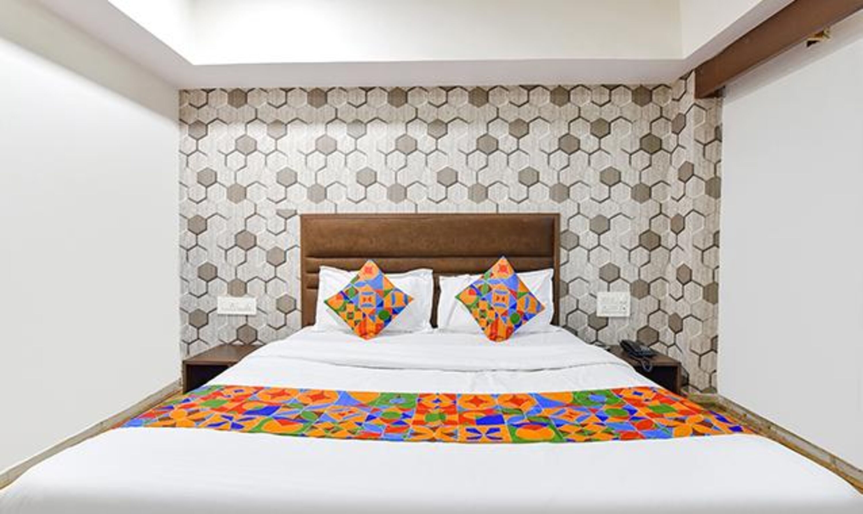 Quarto de hotel com cama, cabeceira de madeira e parede estampada.