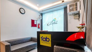 Uma área de recepção de hotel com balcão, dois sofás, um relógio e uma janela com persianas.