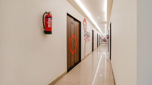 Um corredor limpo e bem iluminado, com um extintor fixado na parede, uma porta com um logotipo circular e uma placa que promove um ambiente sem stress.