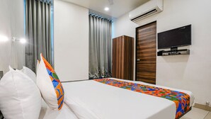 Quarto de hotel com cama, televisão fixada na parede e porta de madeira.