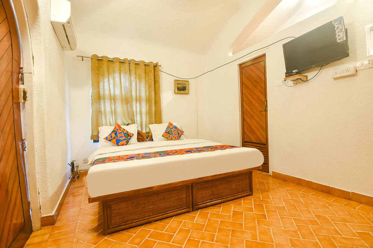 Quarto com cama, televisão na parede e janela com cortinas.