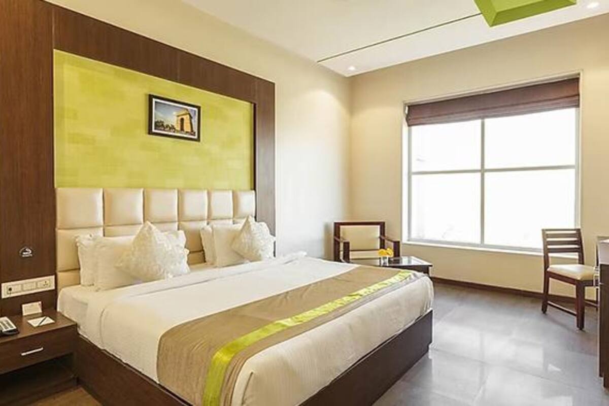 Quarto de hotel com uma cama grande, mesa de cabeceira com abajur, uma cadeira e janela com vista.