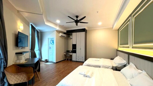 Quarto de hotel com duas camas, uma escrivaninha, uma cadeira, uma televisão e um ventilador de teto.