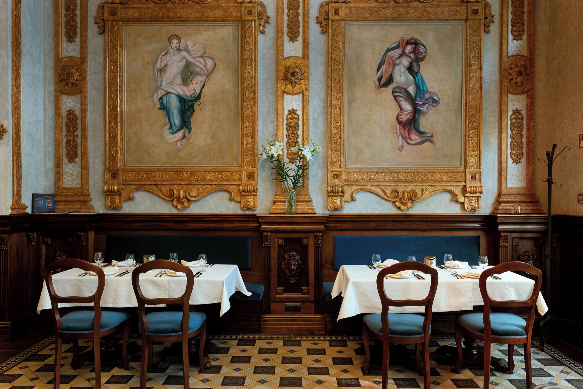 Uma sala de jantar com pinturas elaboradas, cadeiras de madeira e mesas postas para uma refeição.