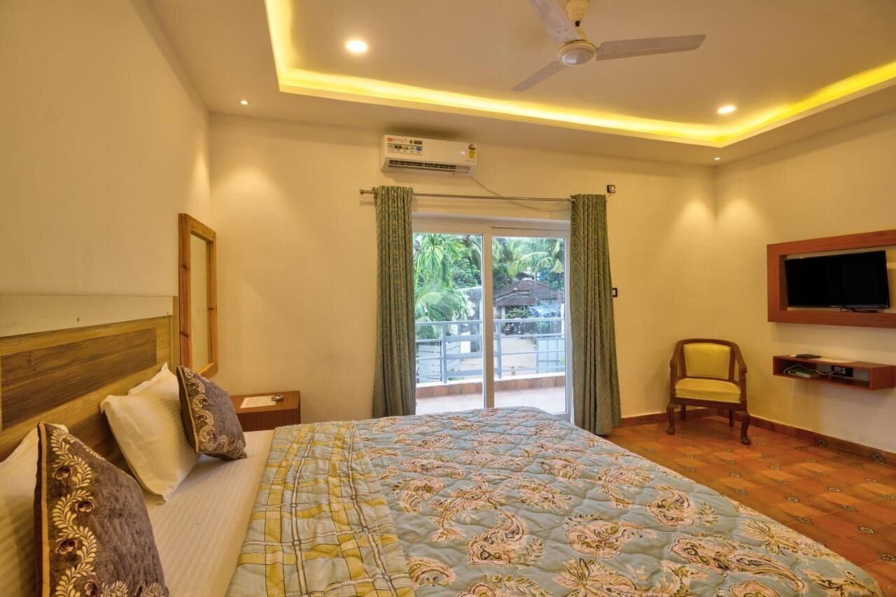 Quarto com cama, ventilador de teto, ar condicionado, TV fixada na parede e vista para o exterior por uma porta de correr.