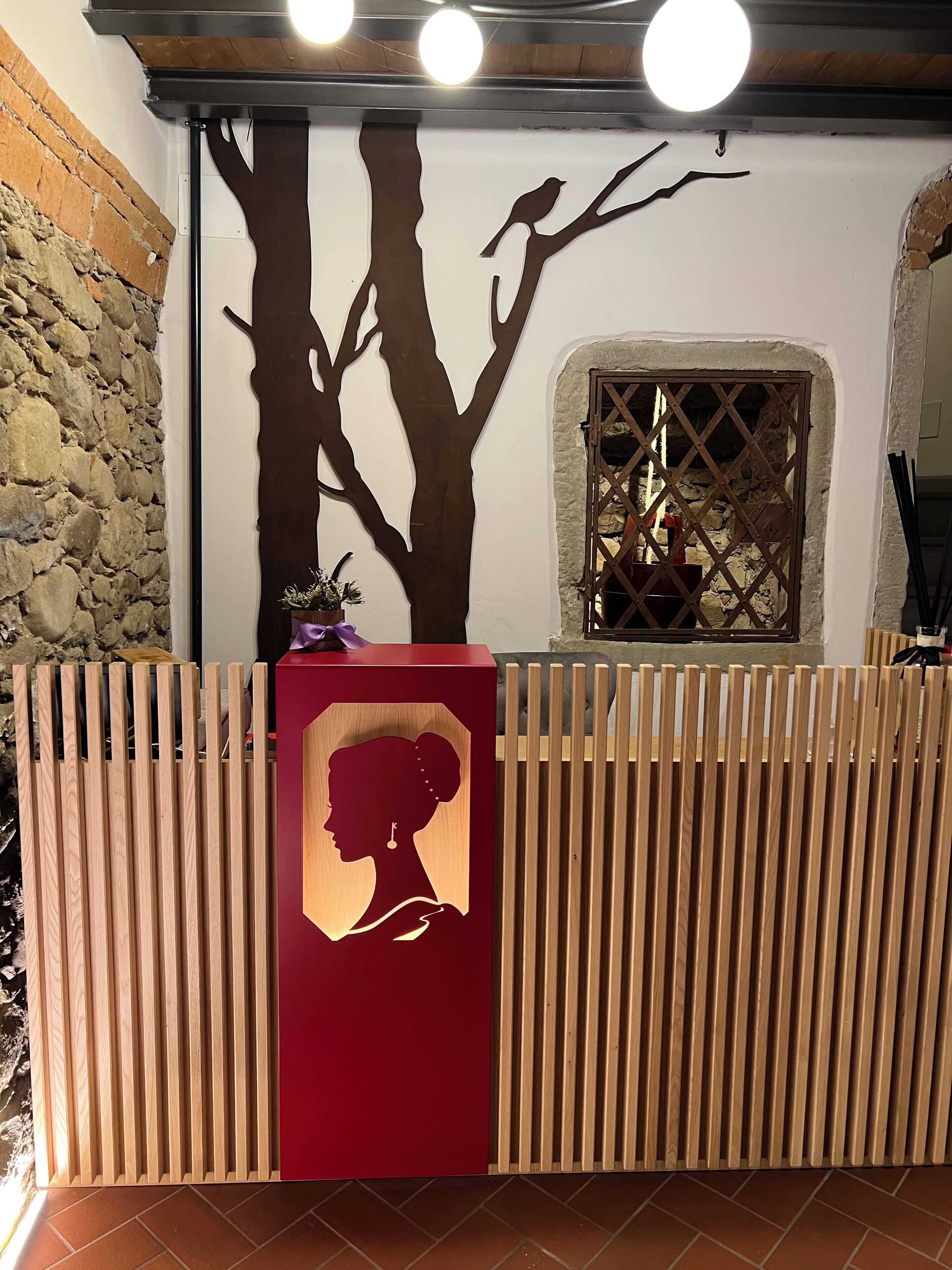 Uma receção com design em ripas de madeira, um painel vermelho com silhueta, parede de pedra e janela com padrão treliçado.