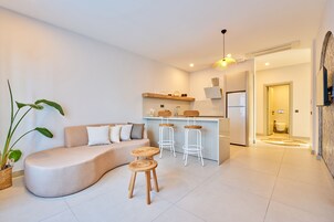 Uma sala de estar moderna com um sofá curvo, dois banquinhos de vime e uma área de cozinha com balcão.