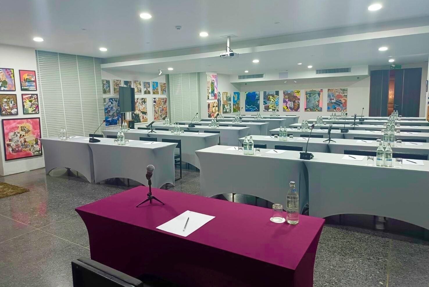 Uma sala de conferências com várias mesas, um púlpito e obras de arte nas paredes.