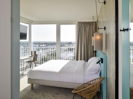 Quarto com uma cama grande, uma cadeira, uma televisão e uma varanda com vista para a cidade.