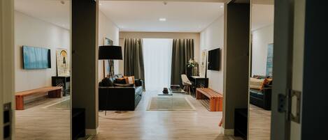 Quarto de hotel moderno com piso de madeira, um sofá, uma mesa de centro e uma televisão.
