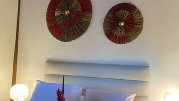 Quarto de hotel com uma cama, duas decorações na parede, uma luminária e uma mesinha de cabeceira.