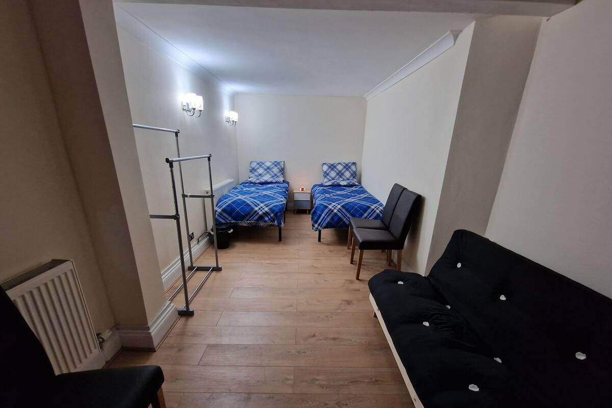 Quarto pequeno e estreito com duas camas, uma cadeira, um radiador e uma prateleira.