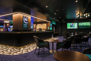 Um espaço de bar moderno com balcão, assentos e telas exibindo jogos esportivos.