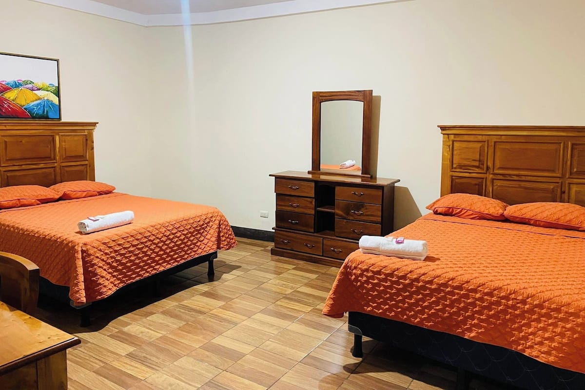 Quarto de hotel com duas camas, cabeceiras de madeira, cômoda com espelho e um quadro na parede.
