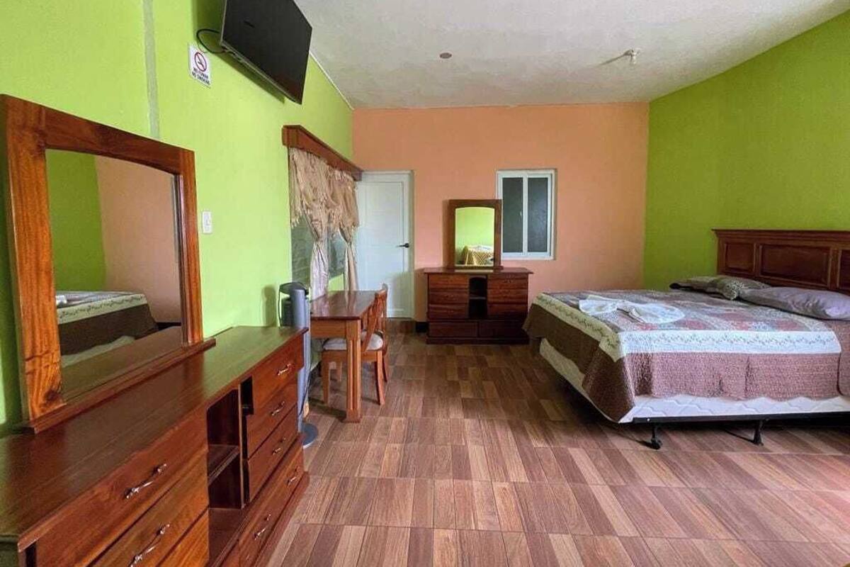 Quarto com cama, penteadeira de madeira, televisão na parede e janela.