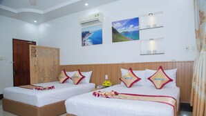 Quarto de hotel com duas camas, um guarda-roupa de madeira, ar condicionado fixado na parede e quadros com paisagens.