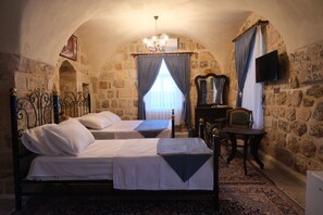 Quarto com duas camas, um lustre, paredes de pedra, uma televisão e um espelho.