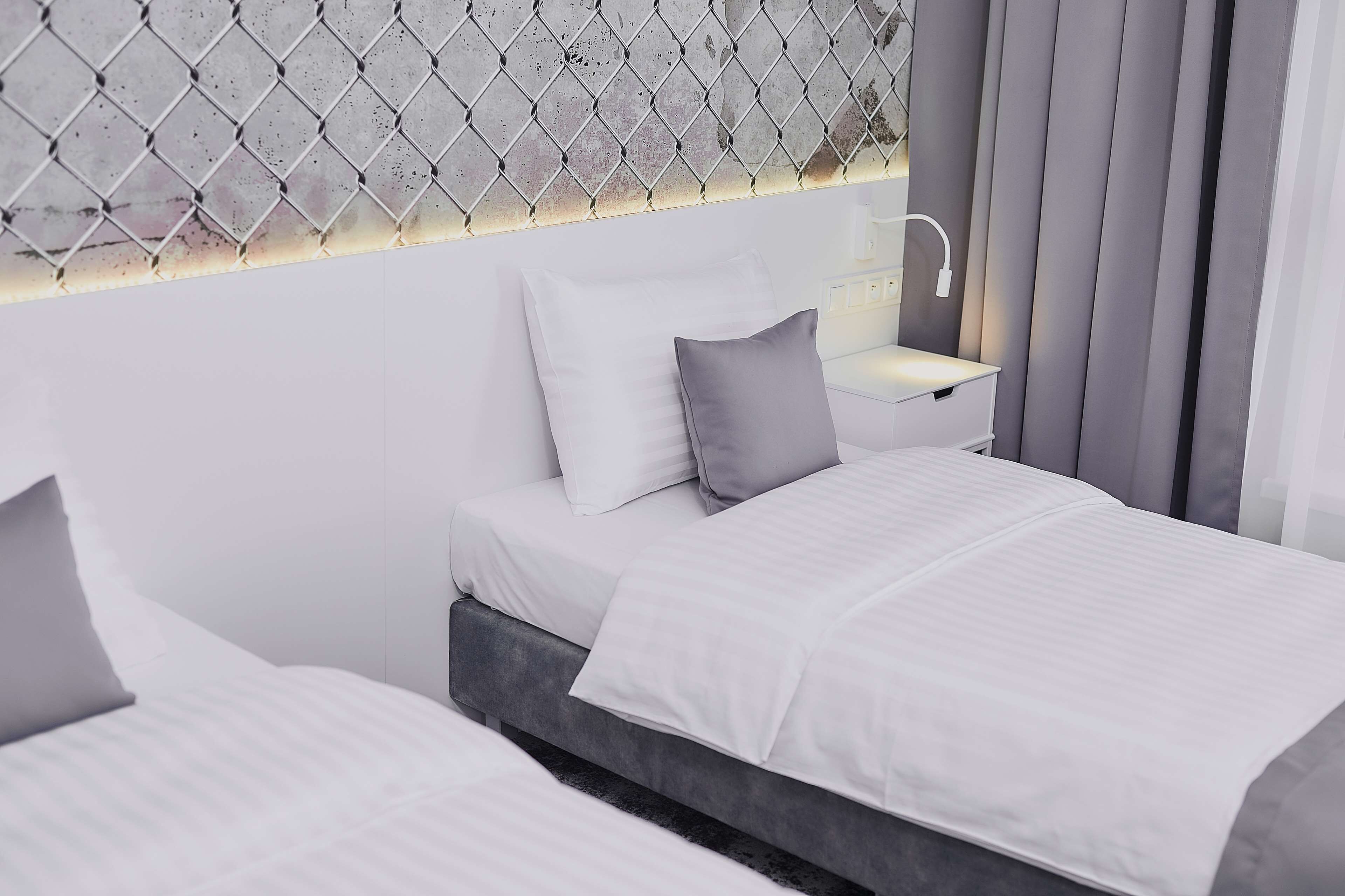 Quarto moderno com cabeceira cinza, roupa de cama branca e mesa de cabeceira com abajur.