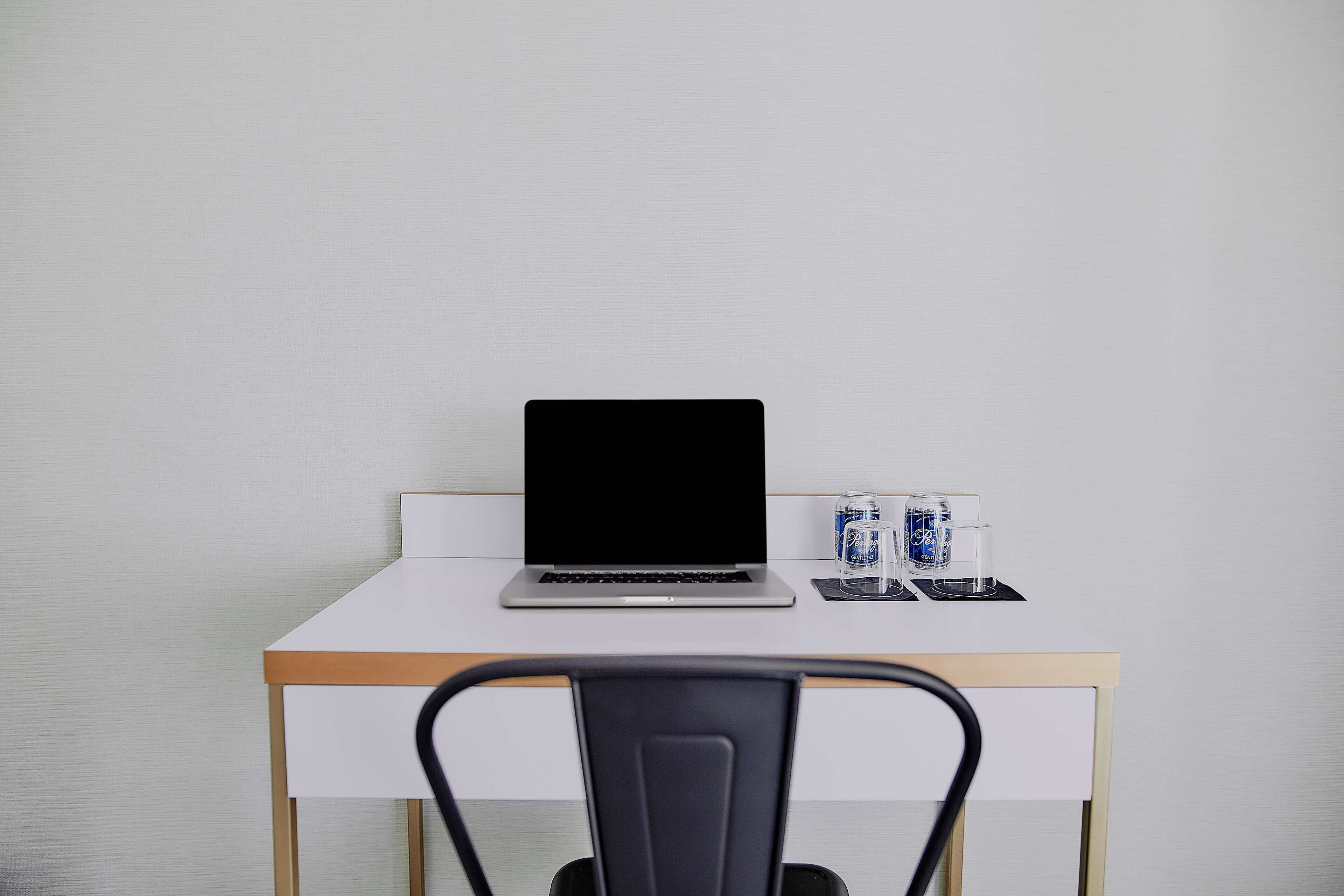 Uma escrivaninha branca com um laptop, duas taças de água e uma lata de refrigerante.
