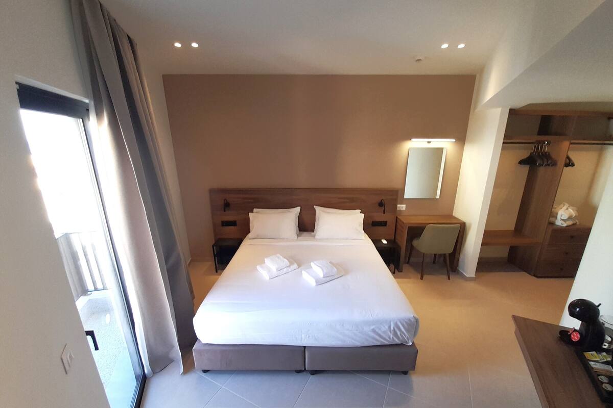 Quarto de hotel com cama grande, escrivaninha, cadeira, espelho e guarda-roupa.