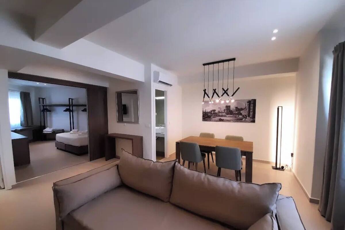Uma sala de estar moderna com sofá, área de jantar com mesa e cadeiras, luminária pendente e pintura de paisagem urbana na parede.