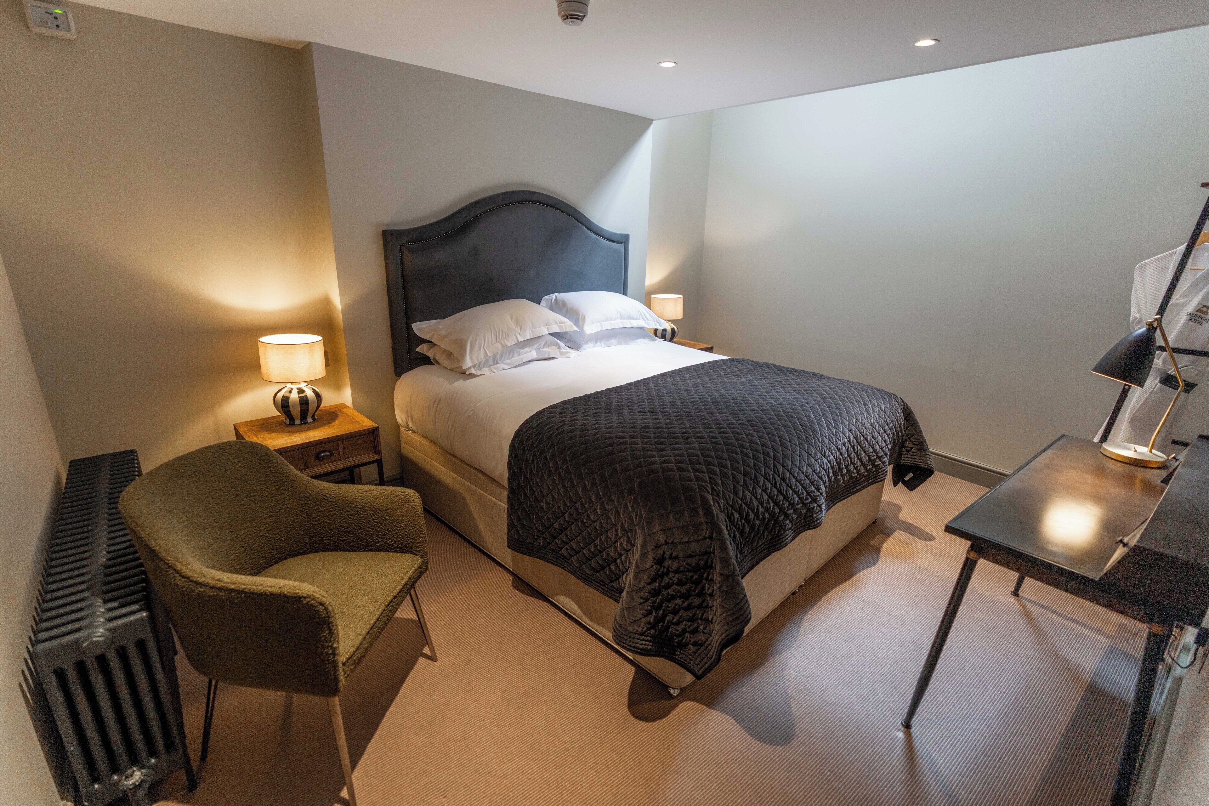 Quarto de hotel com cama, uma cadeira, uma mesa e um abajur.