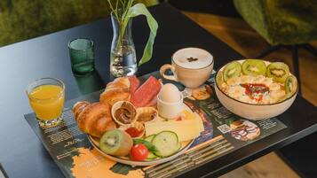 Mesa posta para o café da manhã, com croissants, ovos, kiwi e uma tigela de cereal.