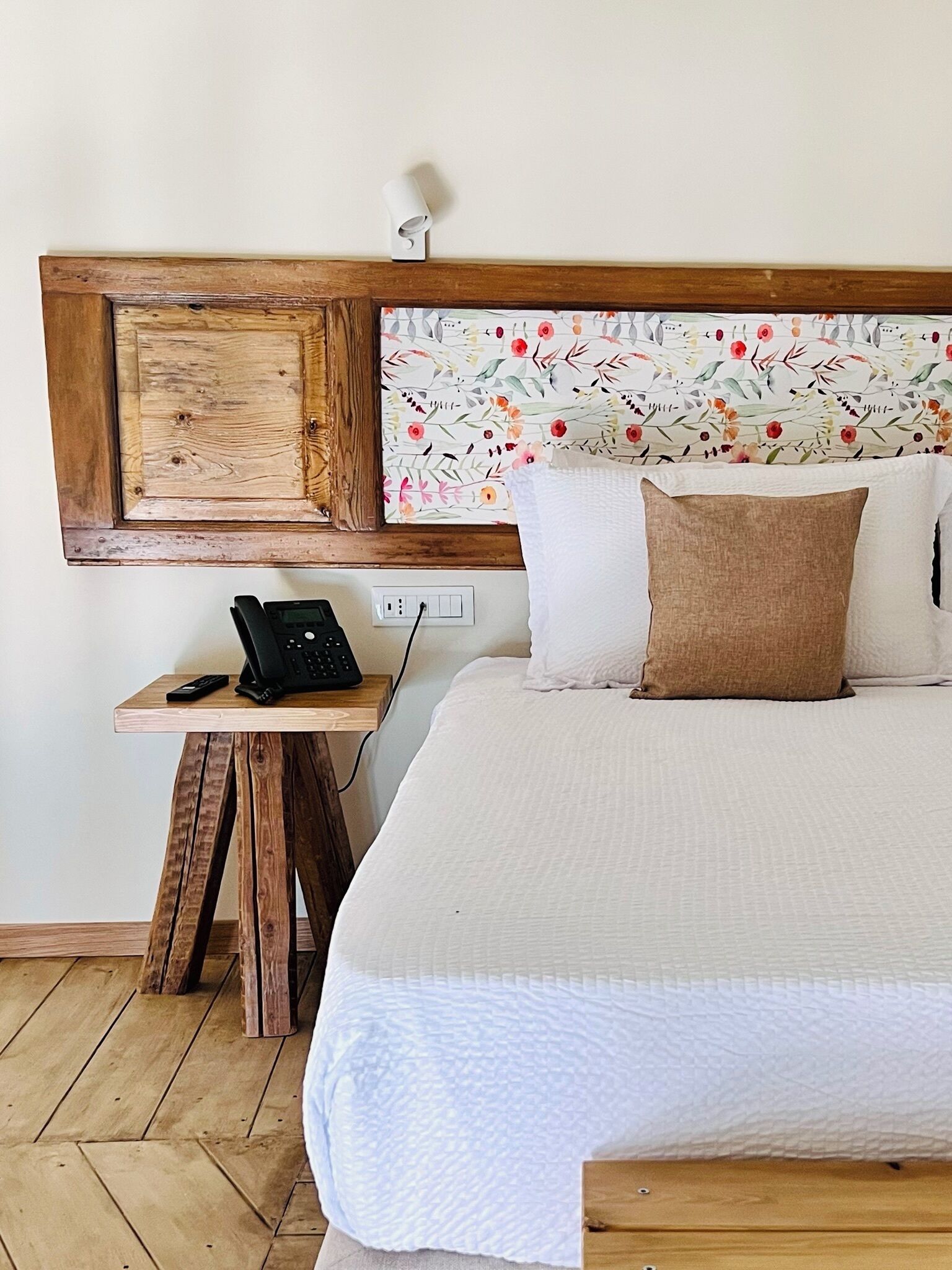 Quarto com cabeceira de madeira, mesa de cabeceira com telefone e cama com almofadas.