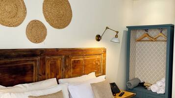 Cama bem arrumada com travesseiros brancos e bege, cabeceira de madeira e três peças de tapeçaria na parede.