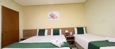 Quarto de hotel com duas camas, cabeceira de madeira, mesa de cabeceira, luminária e quadro pendurado na parede.