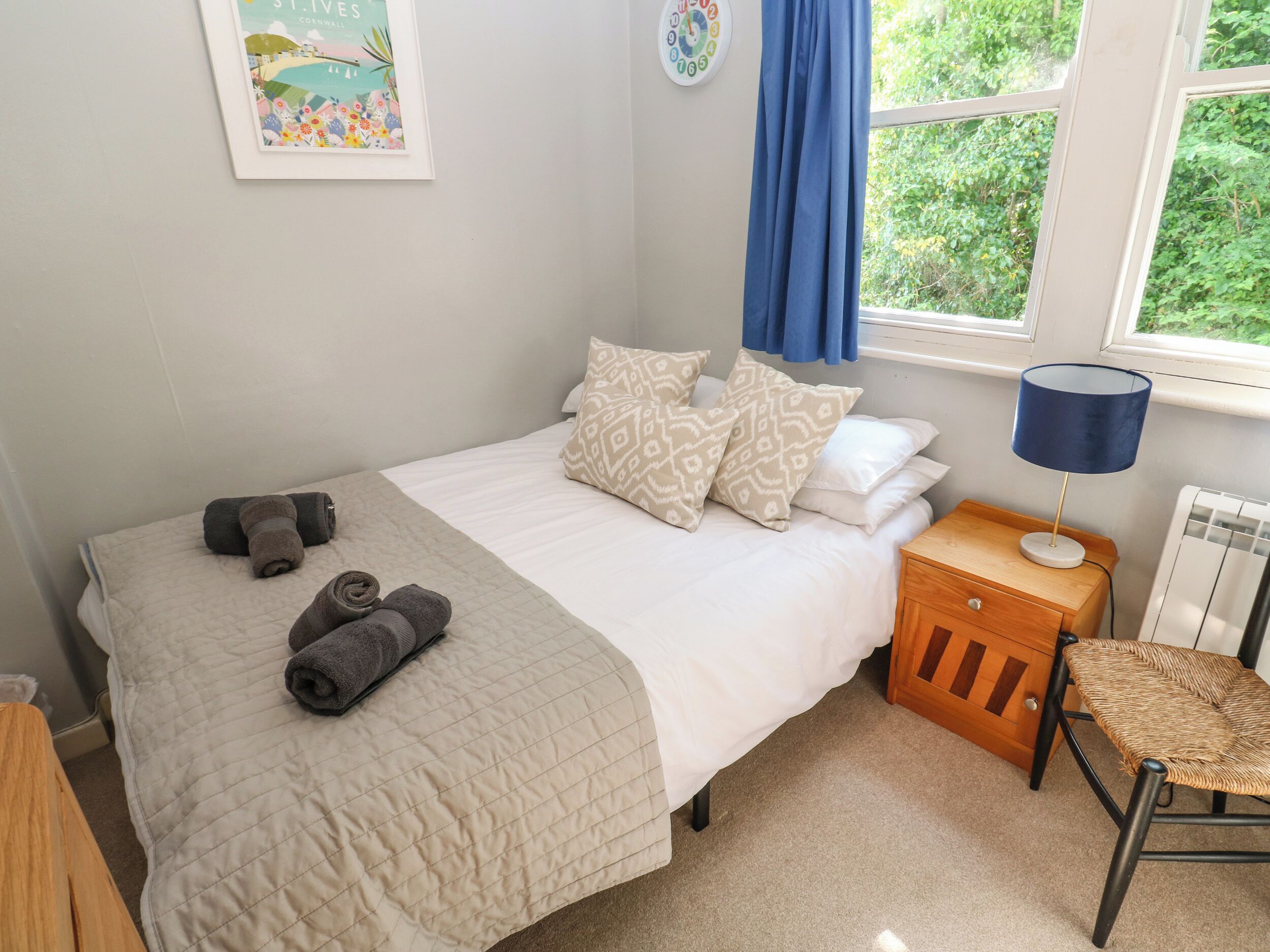 Quarto bem arrumado com cama, travesseiros, mesa de cabeceira com abajur, cadeira e um quadro na parede.