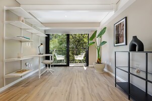 Uma sala de estar moderna com piso de madeira, estantes brancas, um aparador preto e uma grande planta em vaso.