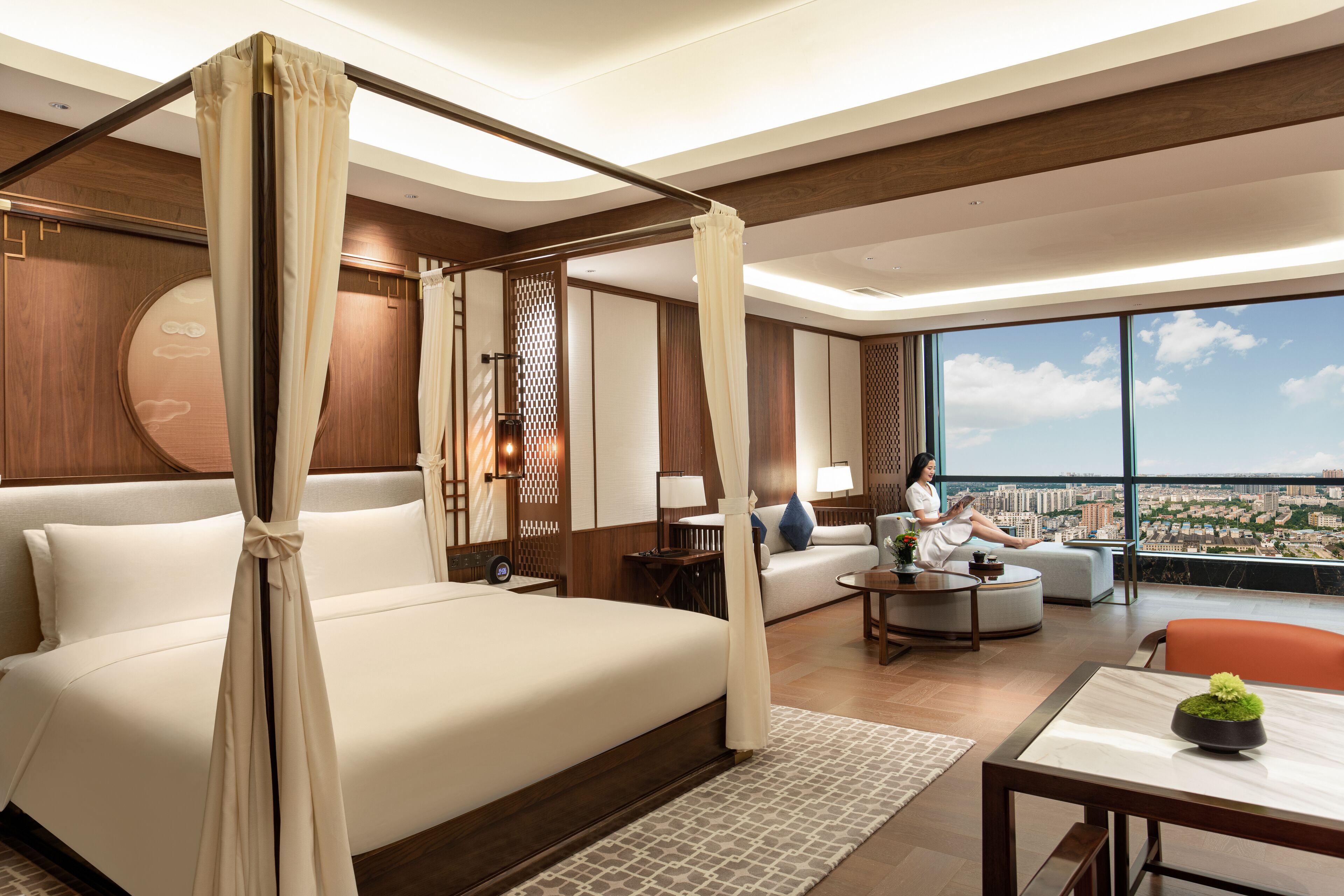 Quarto de hotel moderno com uma cama grande, varanda com vista para a cidade e área de estar com mesa e cadeiras.