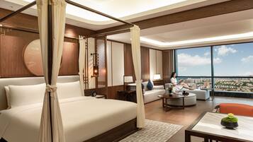 Quarto de hotel moderno com uma cama grande, varanda com vista para a cidade e área de estar com mesa e cadeiras.