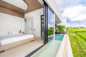 Quarto moderno com uma cama grande, porta de vidro que dá para uma piscina e vista de uma paisagem verde exuberante.