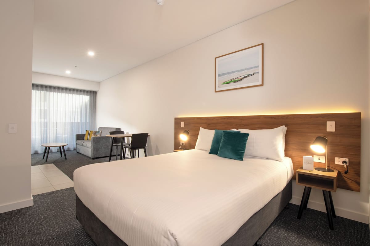 Quarto de hotel com uma cama grande, uma escrivaninha, cadeiras, vista para a praia e um quadro na parede.