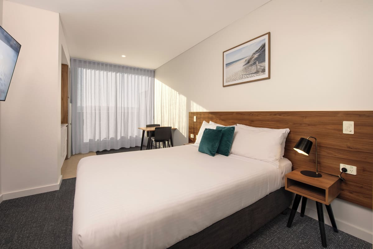 Quarto de hotel com uma cama grande, uma escrivaninha, uma cadeira, uma TV e um quadro na parede.