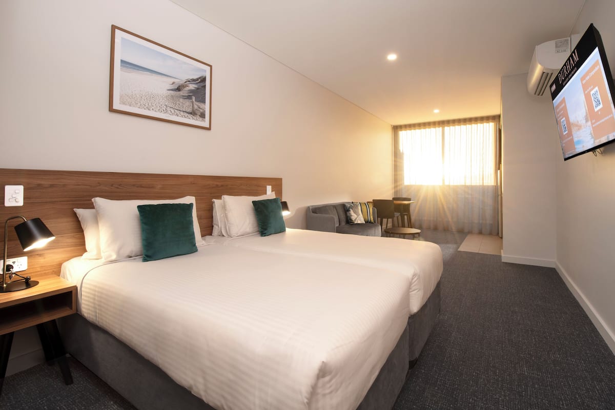 Quarto de hotel com uma cama grande, escrivaninha com luminária, televisão e janela com cortinas.