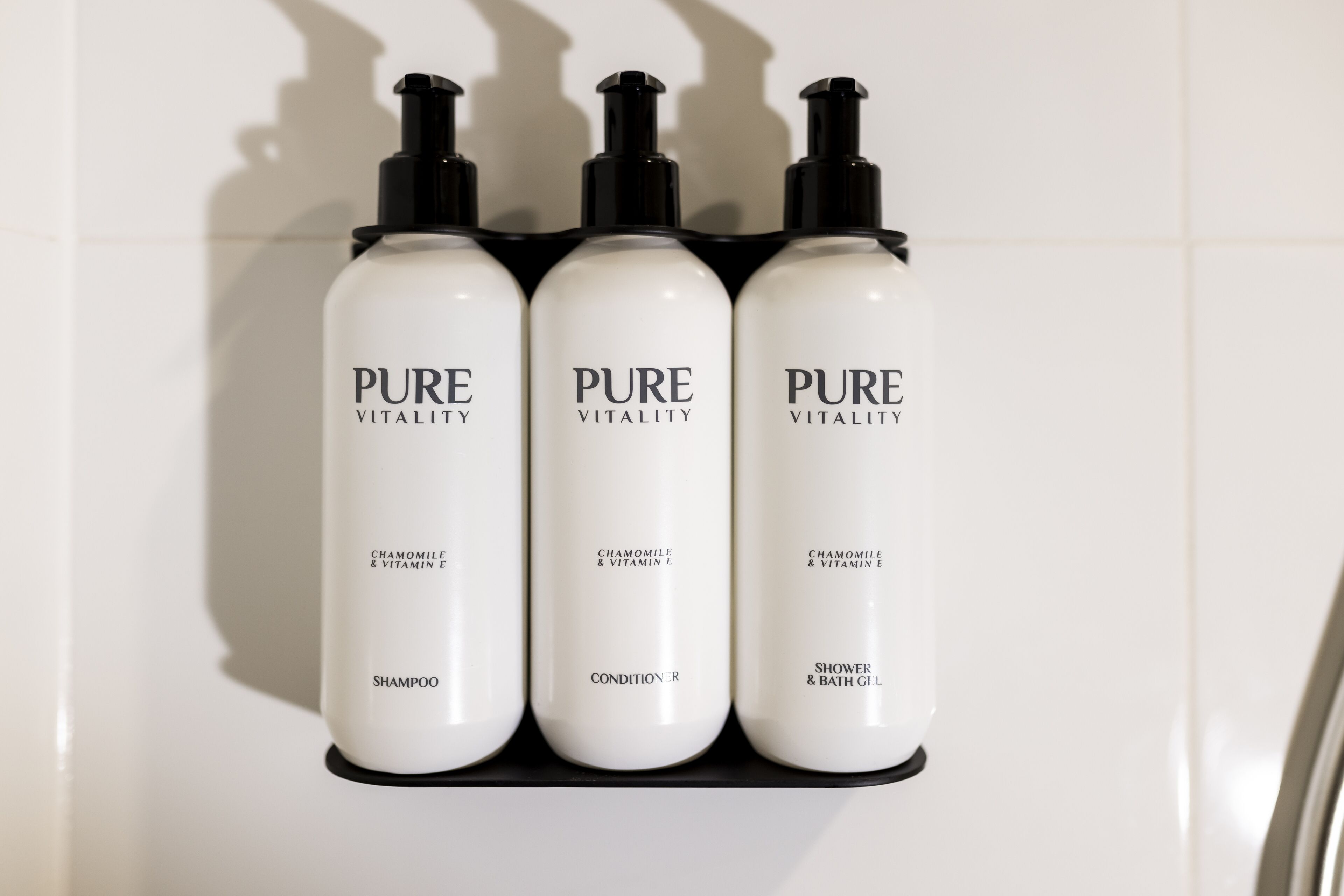 Três frascos de produtos PURE VITALITY: shampoo, condicionador e gel de banho, dispostos sobre uma prateleira branca.