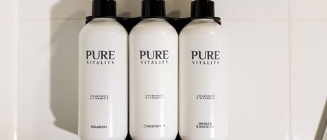 Três frascos de produtos PURE VITALITY: shampoo, condicionador e gel de banho, dispostos sobre uma prateleira branca.