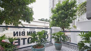 Uma varanda com vasos de plantas, piso de azulejos e vista para um edifício com 'BIR' visível na janela.