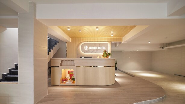 Uma área de recepção de hotel moderna, com um balcão curvo, uma escada à esquerda e um design minimalista.
